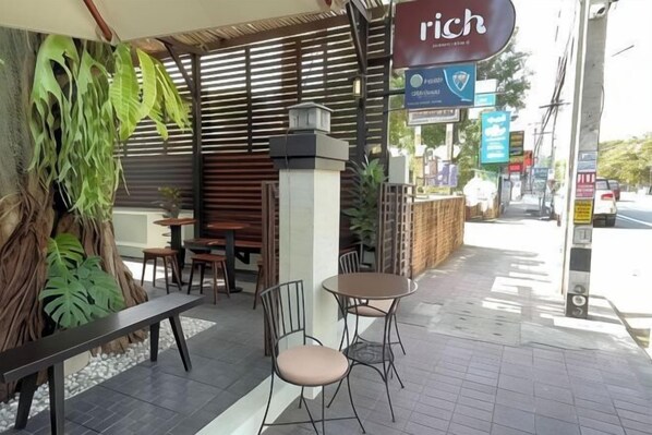 Uma área externa com mesas, cadeiras e um banco, e uma placa com a palavra 'rich'.