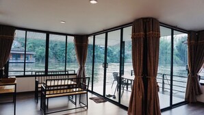 Quarto com uma grande janela com vista para um rio, um banco de madeira e uma mesa com cadeiras.