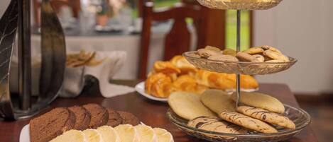 Uma mesa de buffet com diversos produtos de panificação, incluindo bolachas, pastéis e uma sobremesa em camadas.