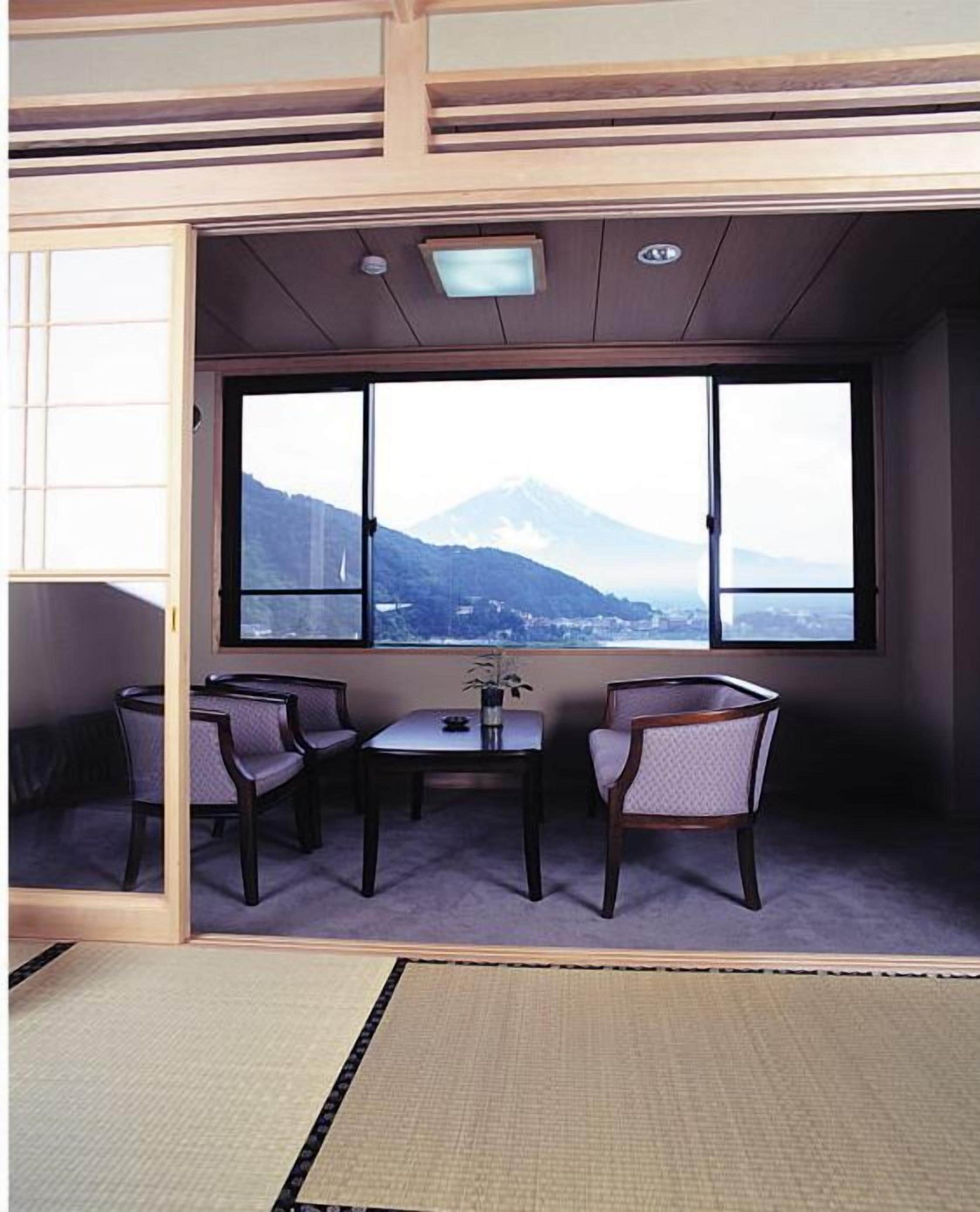 Quarto com piso de tatame, mesa baixa com cadeiras e uma grande janela com vista para as montanhas.
