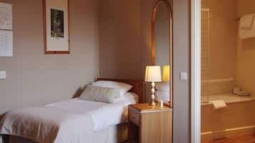 Quarto de hotel com cama, mesa de cabeceira com luminária, espelho e chuveiro.