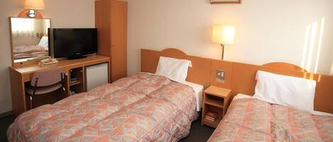 Quarto de hotel com duas camas, uma escrivaninha com televisão, um espelho e um quadro pendurado na parede.