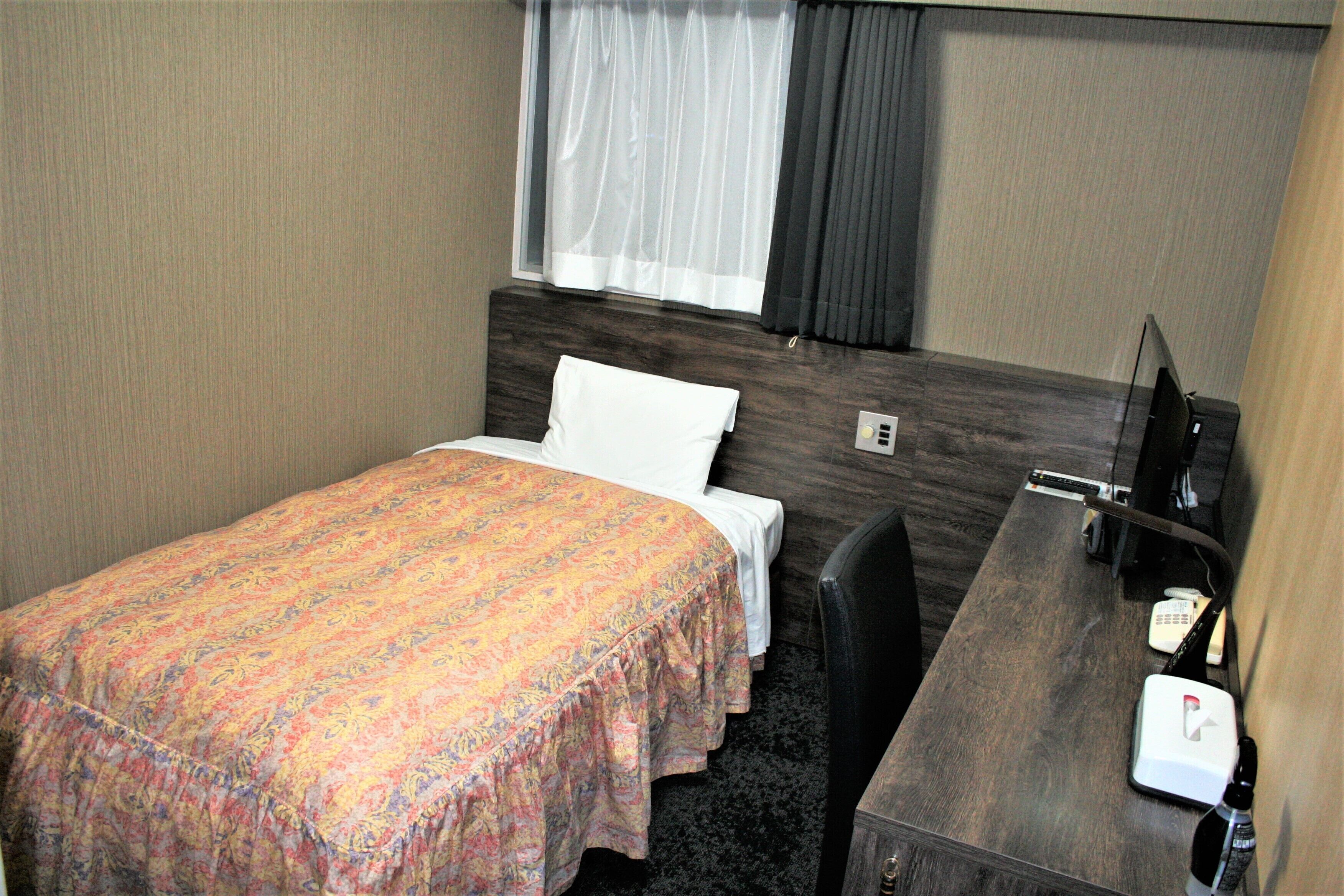 Quarto de hotel com cama, escrivaninha e computador, e janela com cortinas.