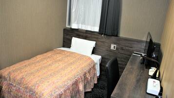 Quarto de hotel com cama, escrivaninha e computador, e janela com cortinas.