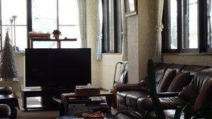 Sala de estar com televisão de tela grande, sofá de couro, mesa de centro e uma pequena árvore de Natal.
