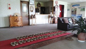 Um lobby com carpete vermelho que conduz a um balcão de recepção, um armário de madeira, um sofá de couro preto e uma fileira de sapatos no carpete.