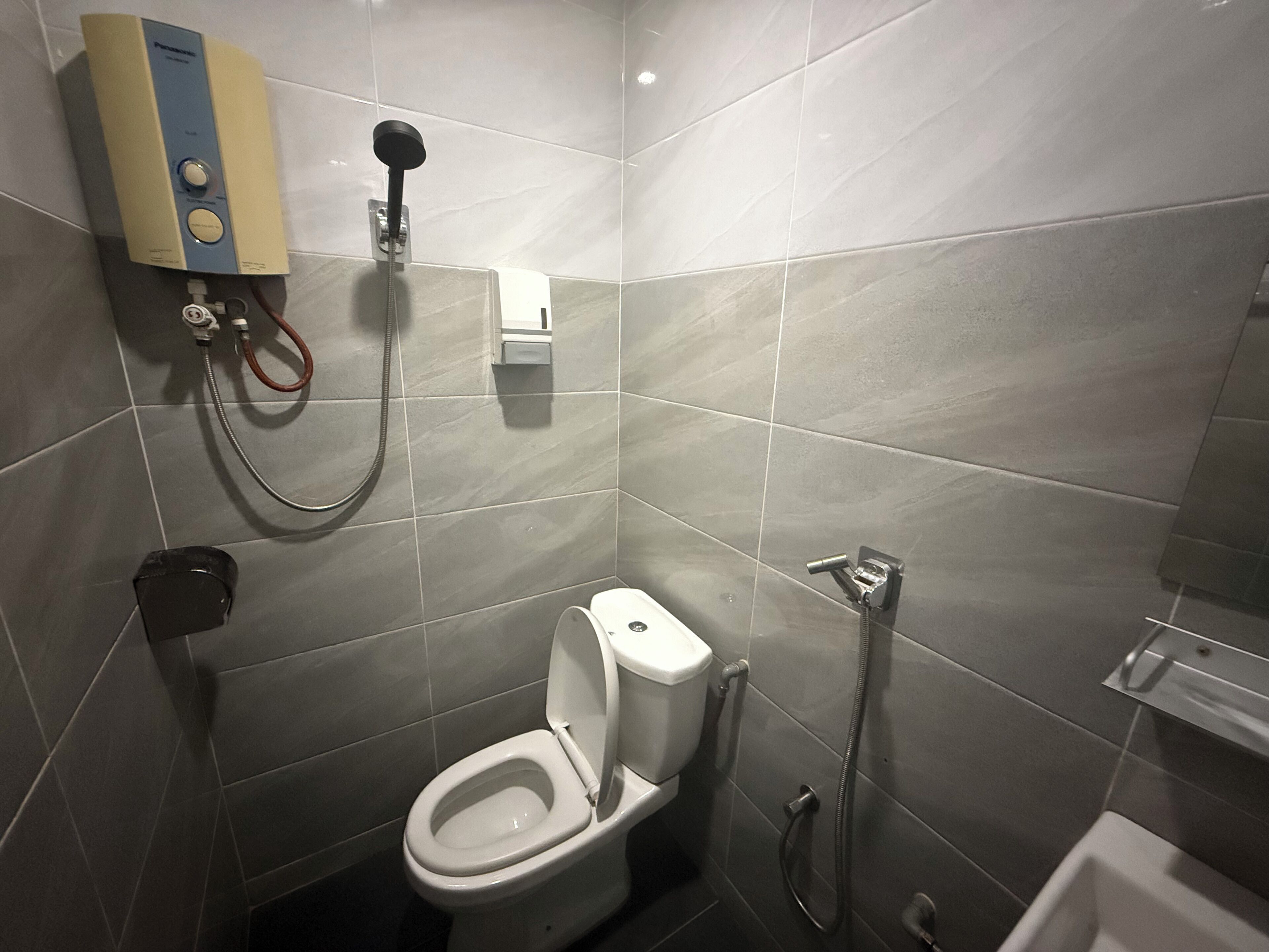 Casa de banho com sanita, chuveiro manual e aquecedor de parede.