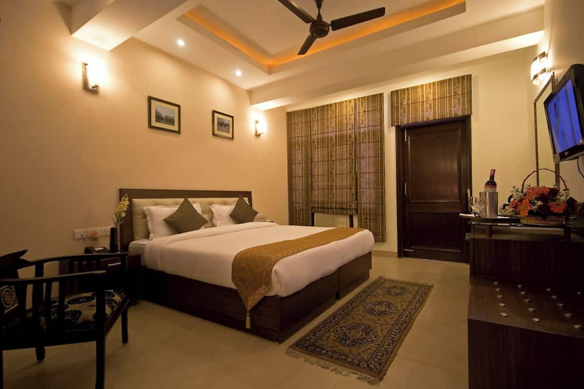 Quarto de hotel com cama, escrivaninha com televisão, ventilador de teto e janela com cortinas.