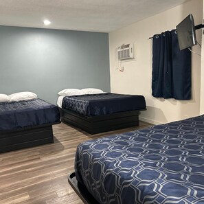 Quarto de hotel com duas camas, televisão de tela plana presa na parede e janela com unidade de ar condicionado.