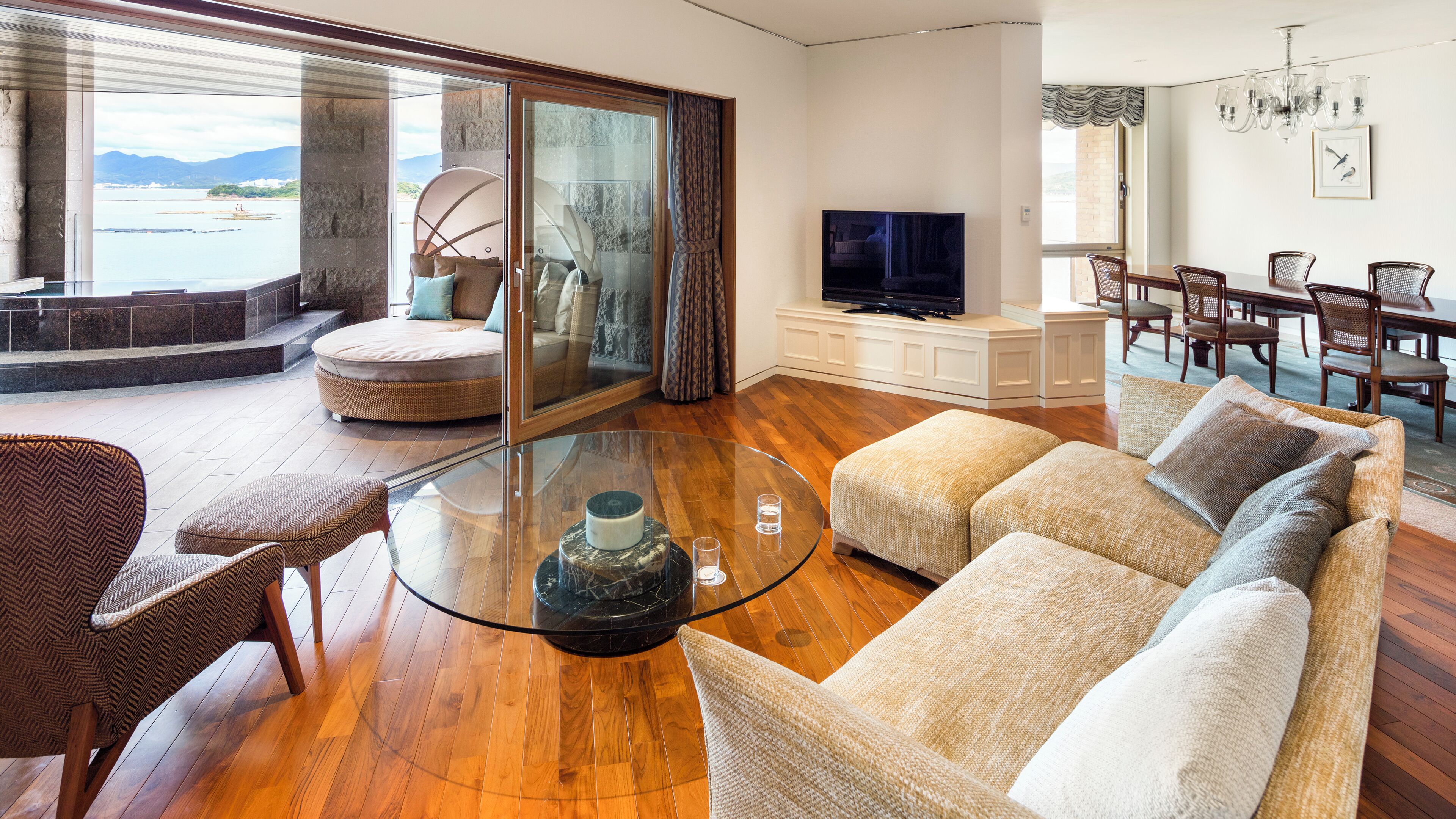 Uma sala de estar moderna com uma mesa de centro de vidro, móveis de vime, uma TV e um espaço de jantar com cadeiras e mesa.