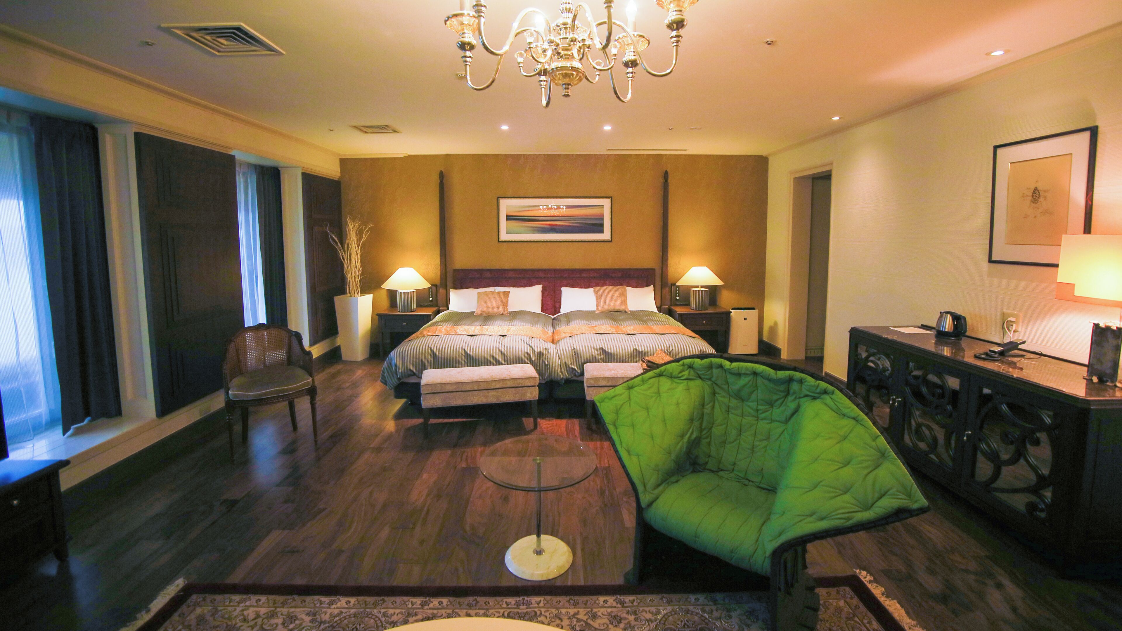 Quarto de hotel com cama grande, duas mesas de cabeceira, uma cadeira, escrivaninha e lustre.