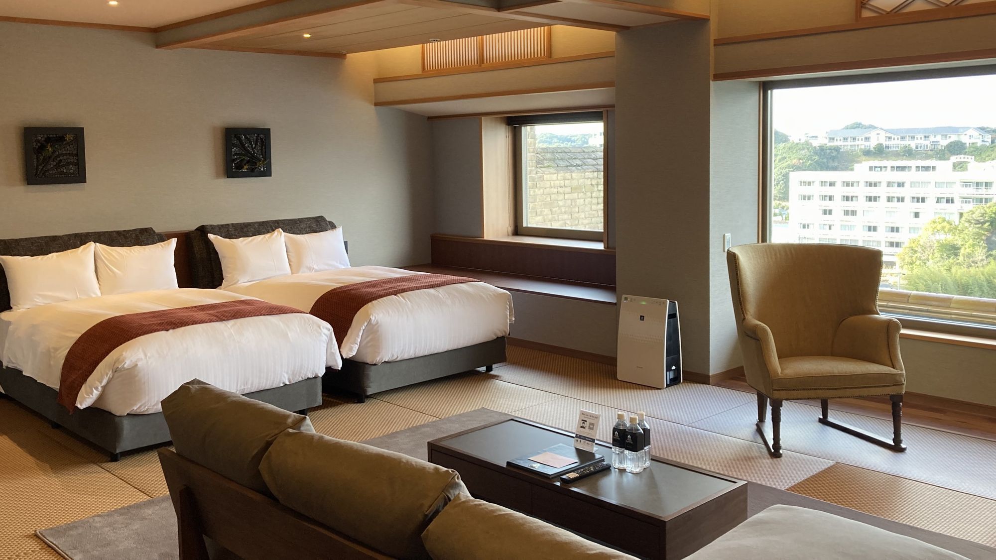 Quarto de hotel com duas camas, um sofá, uma mesa de centro e vista para um edifício.