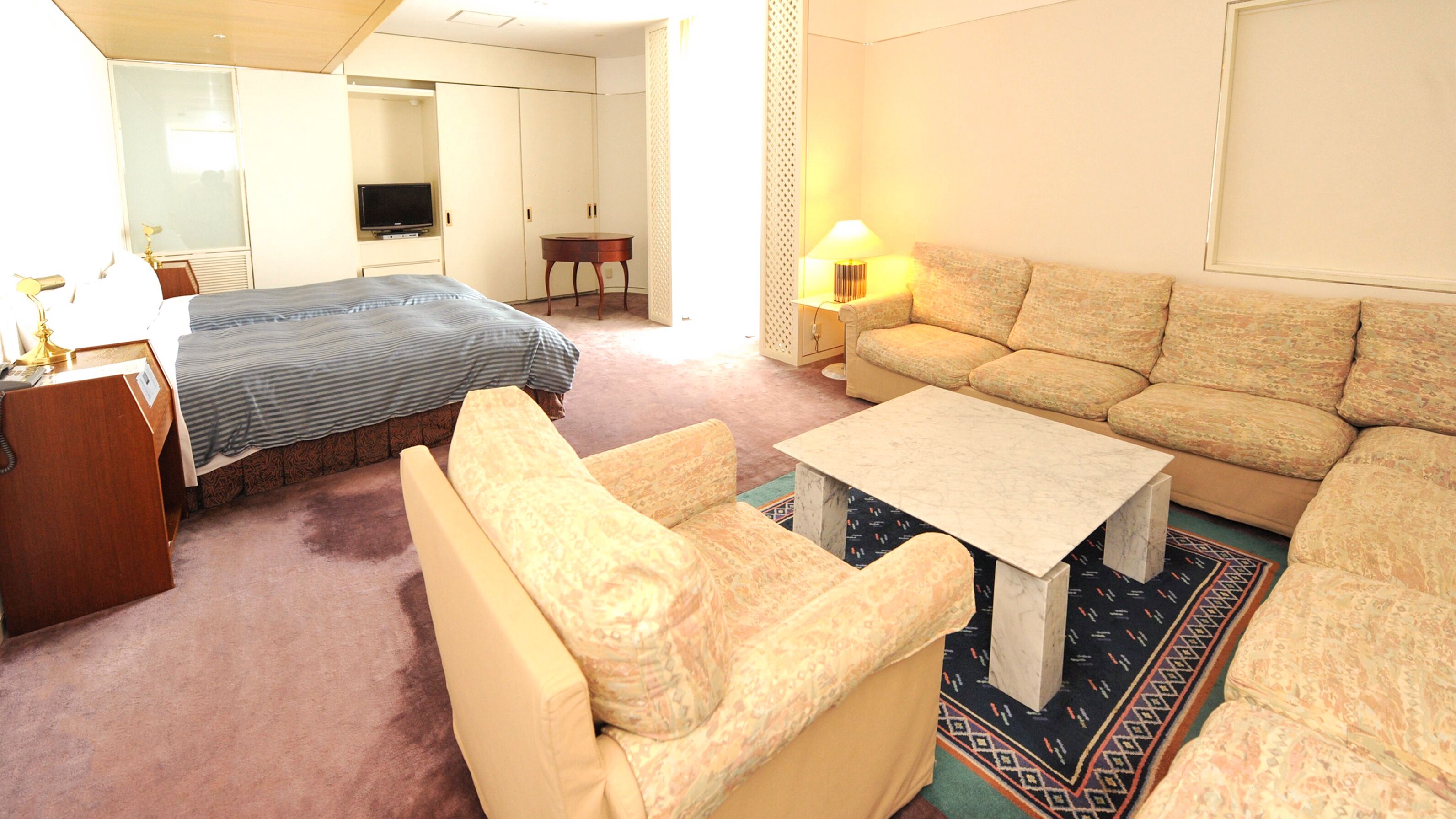 Quarto de hotel com cama, sofá, mesa de centro, televisão e escrivaninha.