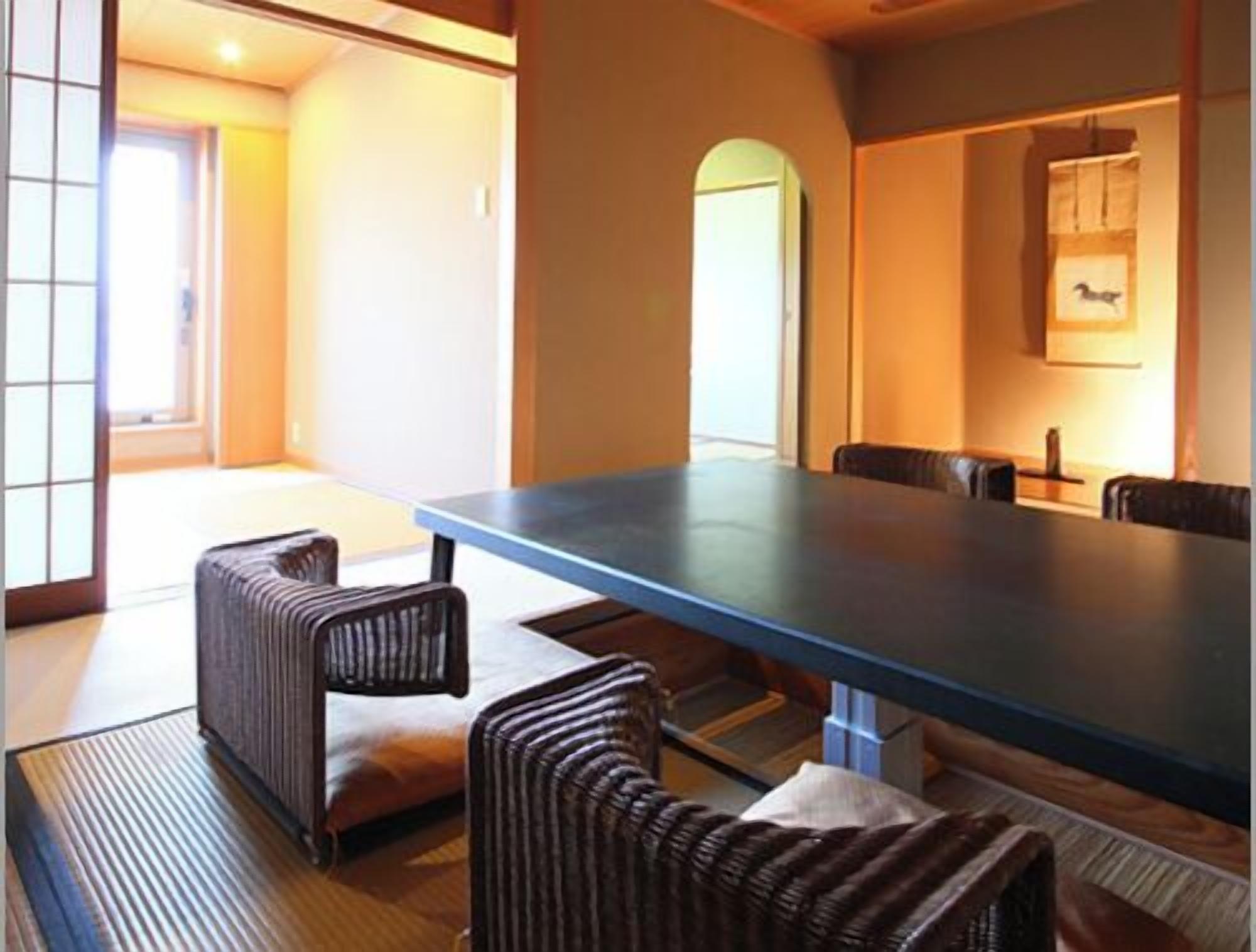 Uma sala de jantar com uma mesa comprida, cadeiras acolchoadas e vista para o exterior.