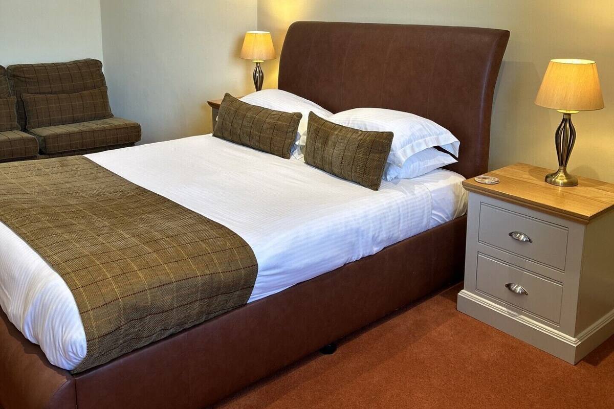 Quarto de hotel com uma cama grande, duas mesas de cabeceira e piso coberto por carpete.