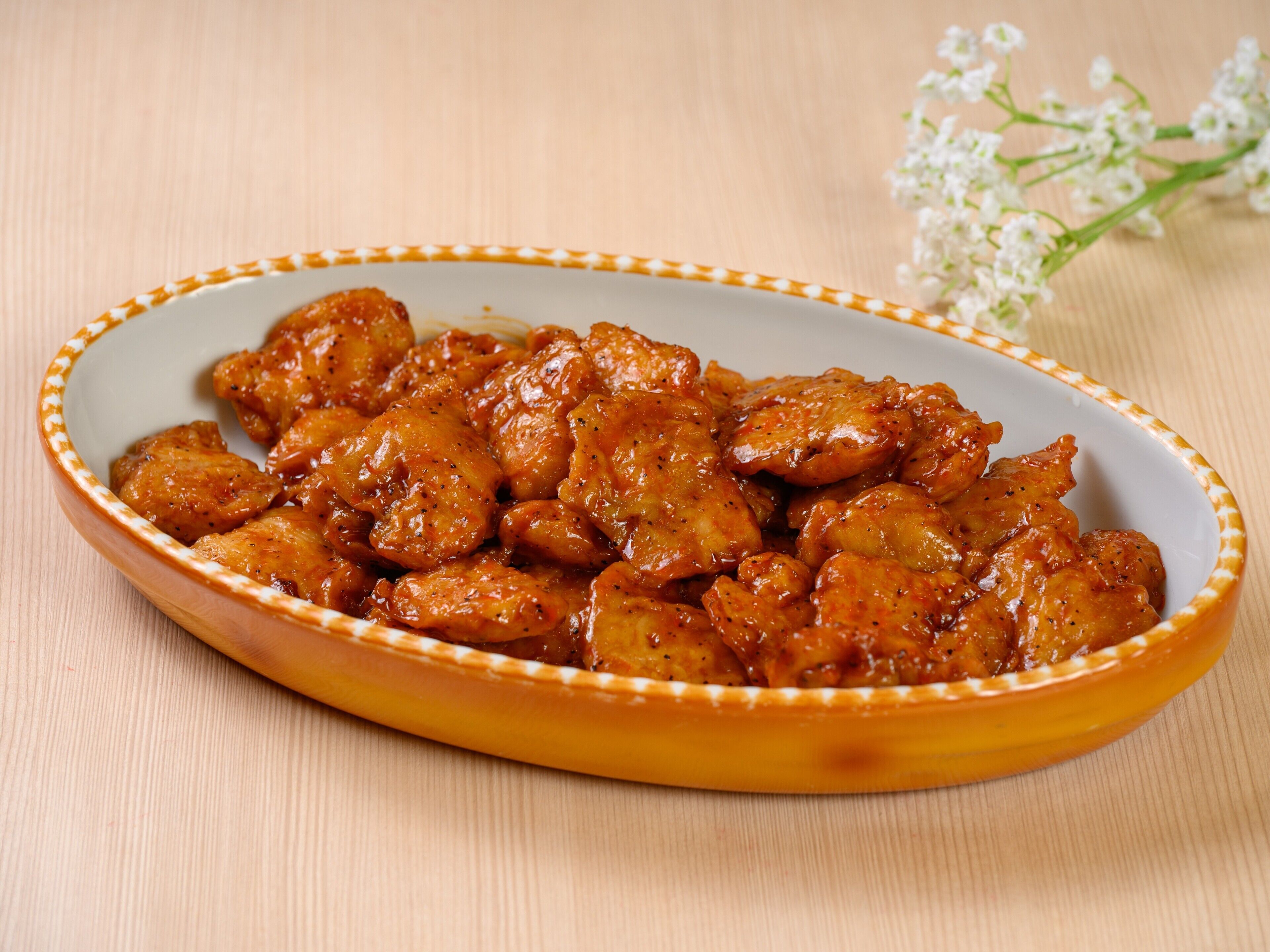 Um prato de asas de frango glaceadas sobre um prato branco com borda amarela.