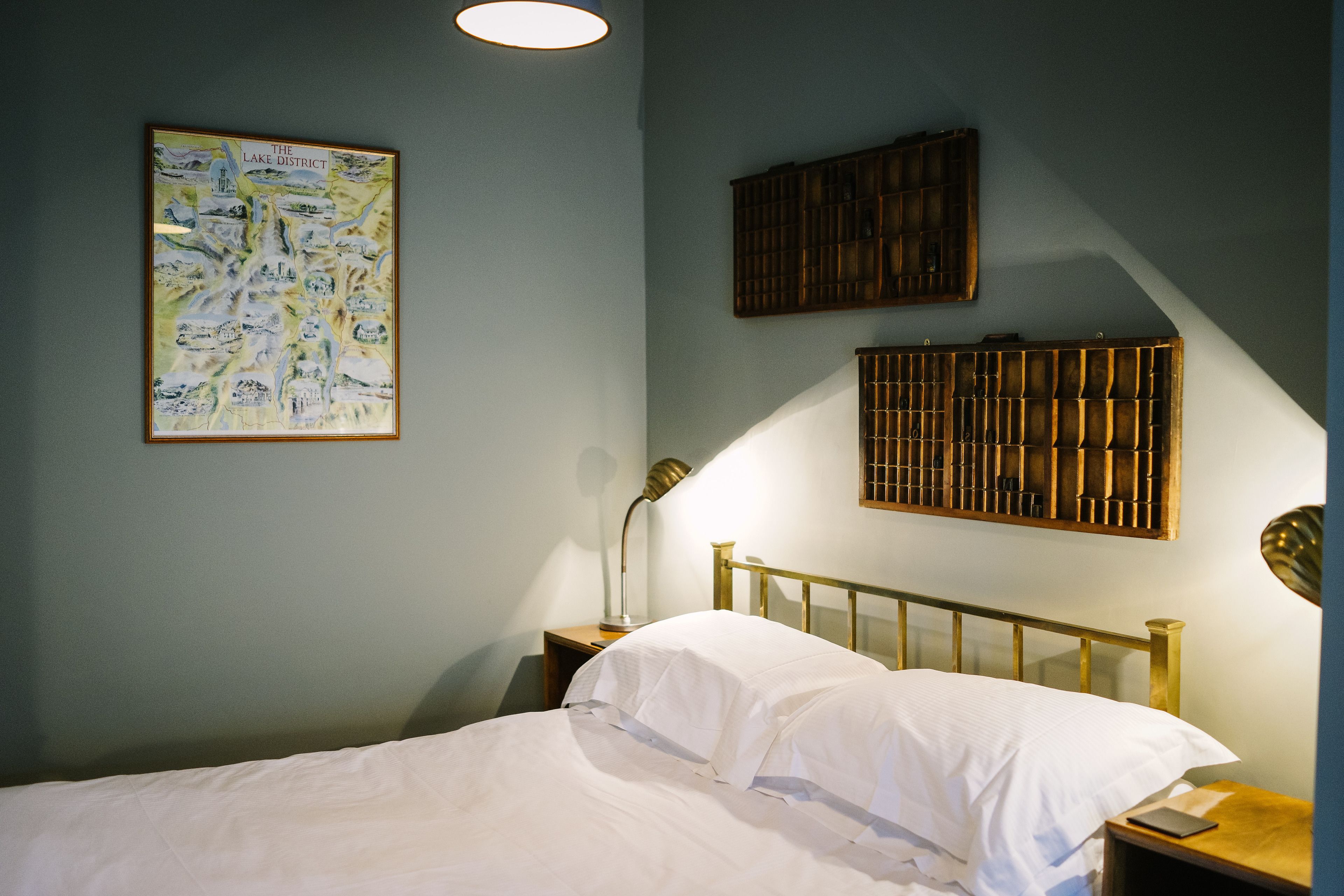 Cama bem arrumada com lençóis brancos, um mapa emoldurado na parede e cabeceira de madeira.