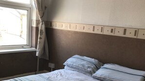 Uma cama com roupa de cama listrada, uma janela com cortinas e uma parede com um painel decorativo.