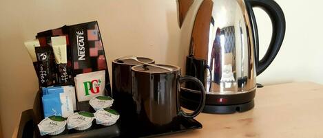 Uma bandeja com cápsulas de café, uma caneca e uma chaleira sobre uma mesa de madeira.