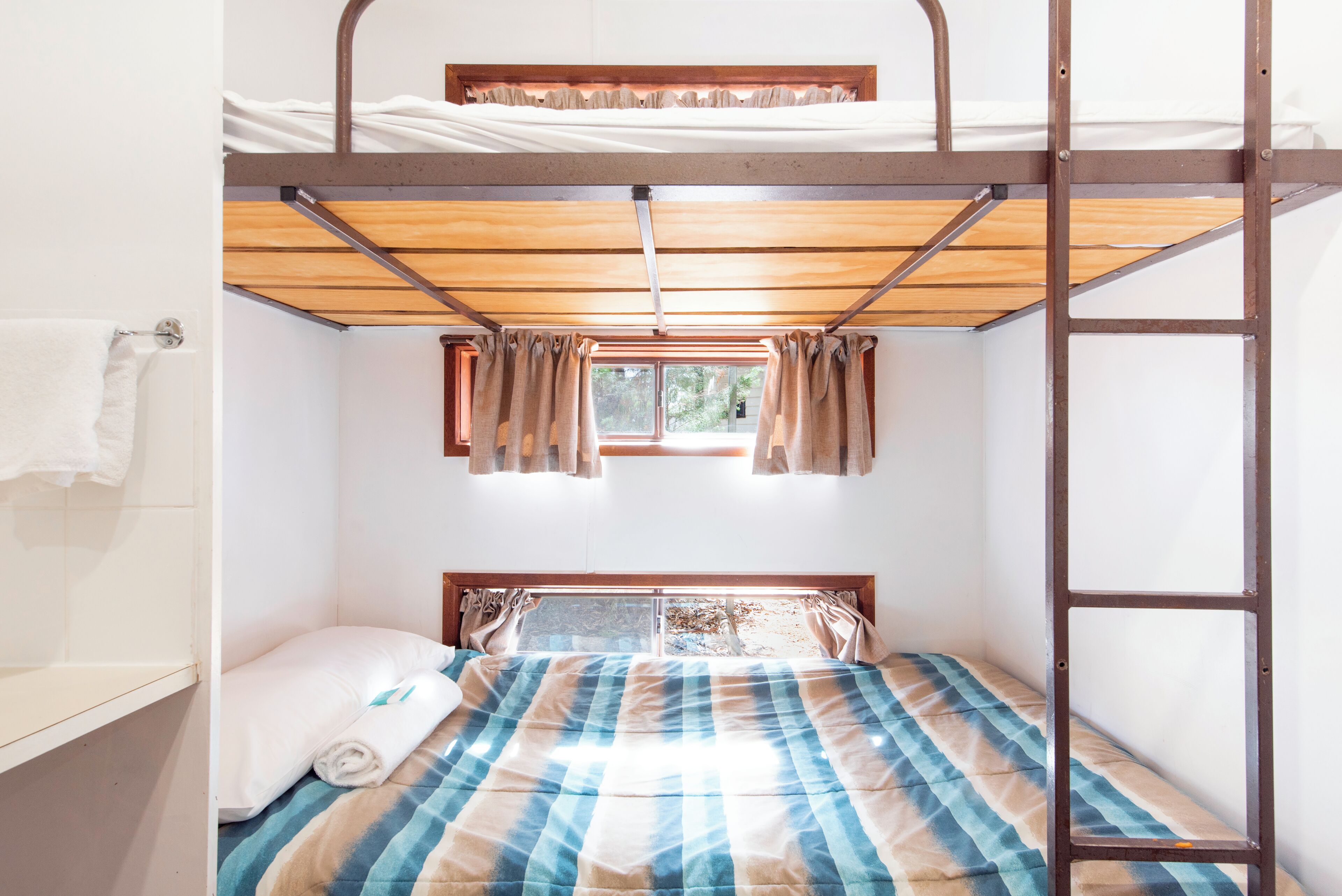 Quarto com beliche, janela, cortinas e porta-toalhas.