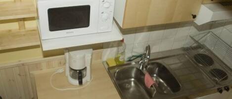 Uma cozinha compacta com micro-ondas, cafeteira, pia e armários de madeira.