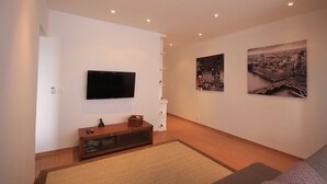Uma sala de estar moderna com televisão de tela plana, móvel de entretenimento de madeira e duas fotografias em preto e branco da paisagem urbana nas paredes.