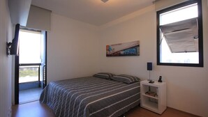 Quarto com cama, mesa de cabeceira, pintura e janela.