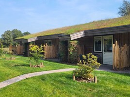 Uma fileira de cabanas modernas com telhados inclinados, cercas de madeira e pequenas árvores na frente.