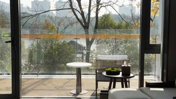 Varanda com porta de vidro, mesa redonda, sofá e vista para árvores e edifícios.