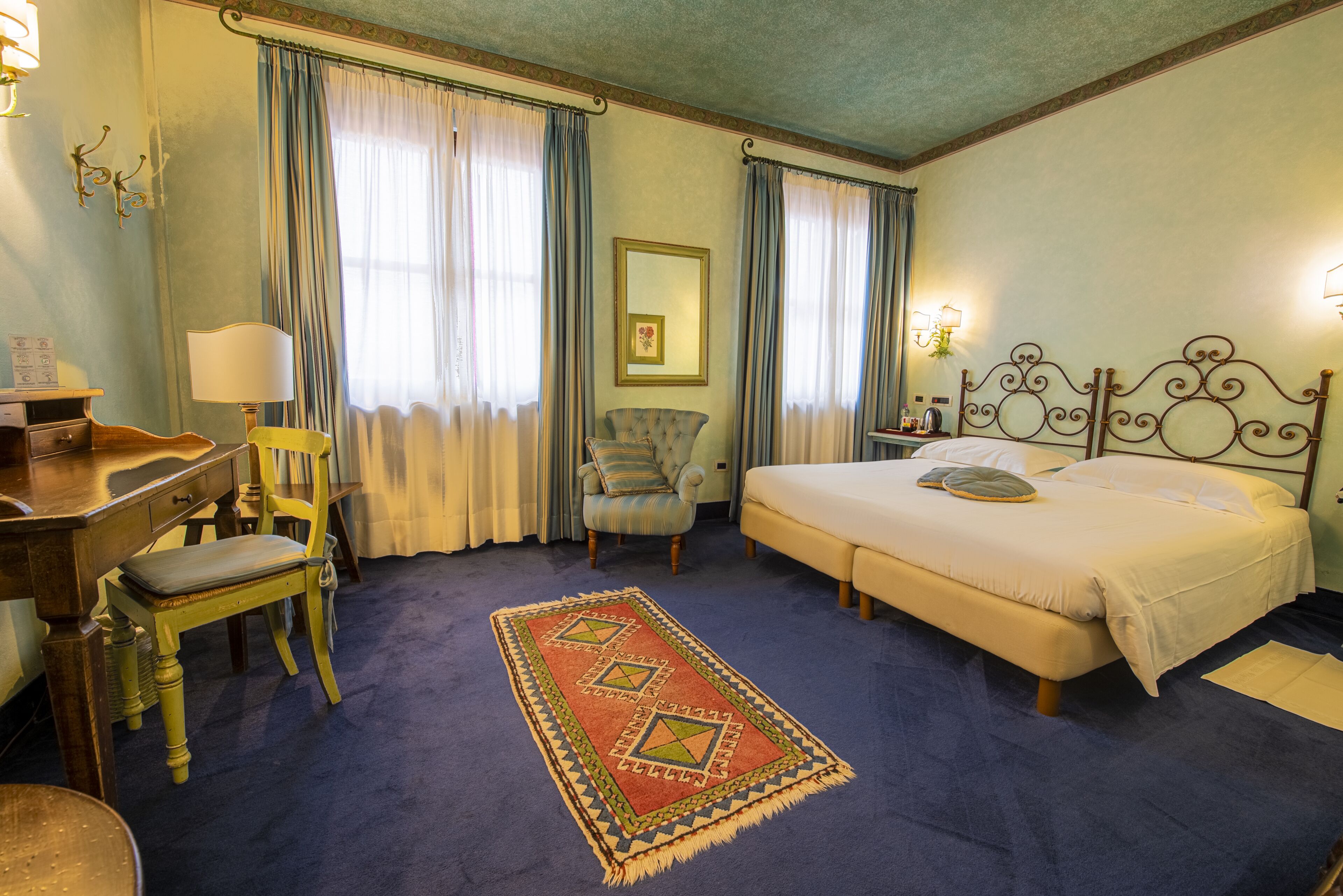 Quarto de hotel com cama, duas cadeiras, uma escrivaninha e um tapete.