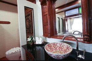 Uma casa de banho com uma bacia de lavatório grande e decorativa, um espelho e uma sanita.