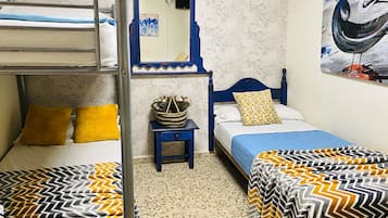 Um quarto de dormitório com beliches, uma mesinha com uma cesta, um espelho e uma cama com roupa de cama estampada.
