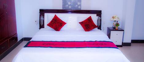 Uma cama com cabeceira de madeira, duas almofadas vermelhas, um cobreleite branco e um tapete corrido vermelho.