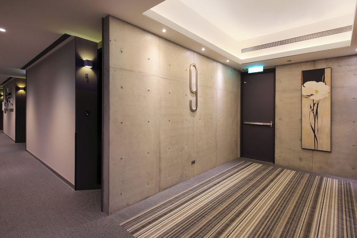 Corredor moderno de hotel com piso coberto por carpete, placa com número fixada na parede e quadro decorativo.