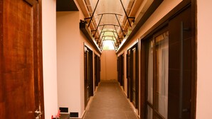 Corredor com portas em ambos os lados, extintor de incêndio à esquerda e teto com luminária geométrica.