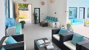 Uma área externa moderna com móveis de vime, uma mesa de centro de vidro e luminárias de rattan suspensas.