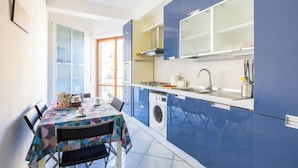 Uma cozinha compacta com armários azuis, uma máquina de lavar e um espaço de jantar com mesa e cadeiras.