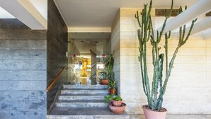 Uma escadaria com corrimão, plantas em vasos e uma placa com a inscrição 'Scala B'.