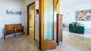 Quarto com porta de madeira, sofá verde, armário de madeira e telefone fixado na parede.