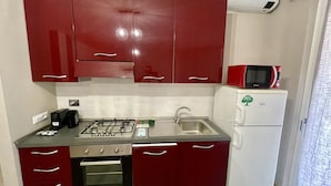 Cozinha compacta com armários vermelhos, fogão a gás, micro-ondas e geladeira.