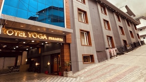 Um hotel com fachada moderna, grandes janelas refletoras e uma placa com a inscrição "OTEL YOGA PREMIUM".
