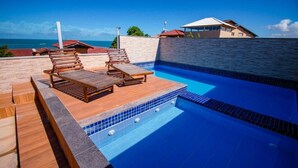 Uma área de piscina com espreguiçadeiras de madeira e vista para o mar.