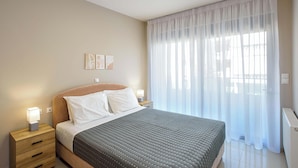 Quarto com cama, mesas de cabeceira e janela com cortinas leves.