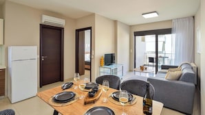 Quarto de hotel moderno com área de refeições, sofá, televisão e varanda com vista.