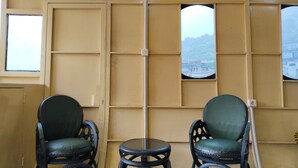 Quarto com duas cadeiras verdes e uma mesa pequena, janela com vista para edifícios e parede com padrão de grade.
