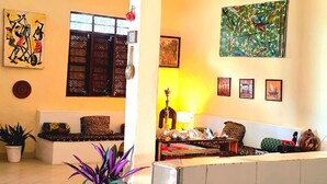 Uma sala de estar espaçosa com pé direito alto, piso ladrilhado e um espaço de estar com almofadas e uma mesa.