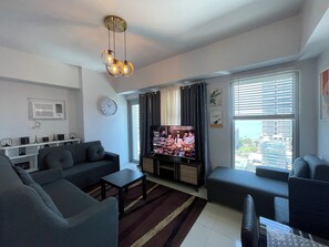 Uma sala de estar moderna com televisão de tela plana, sofás, mesa de centro e uma janela grande com persianas.