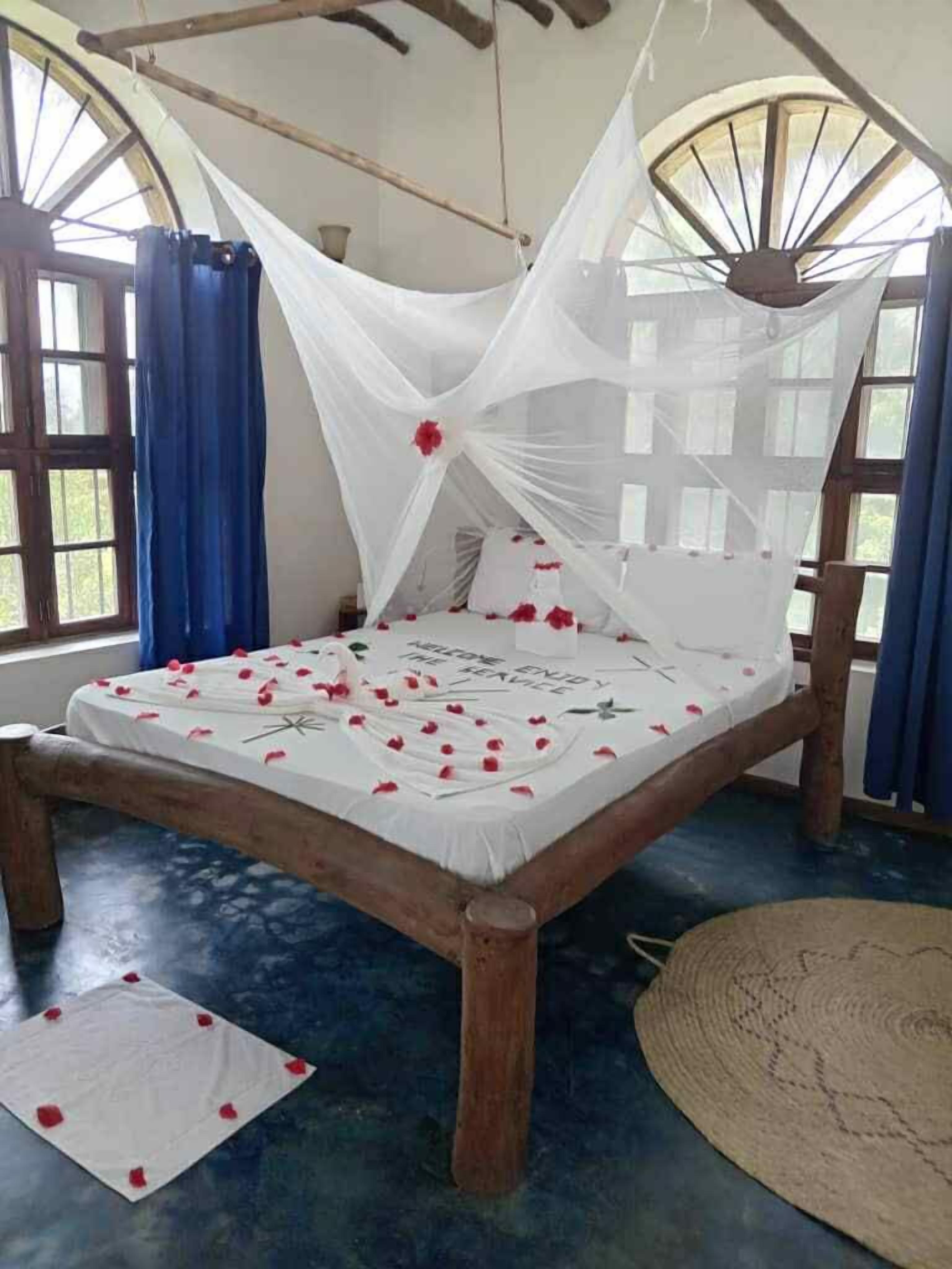 Uma cama com dossel, pétalas de rosa e uma mensagem no cobreleite.
