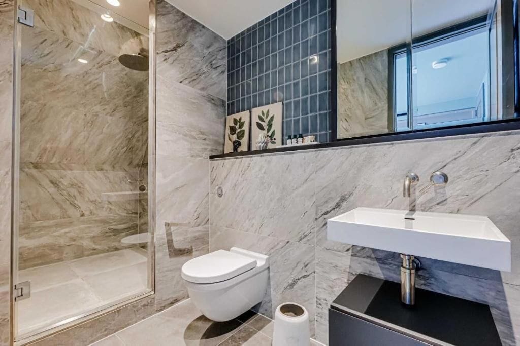Casa de banho com cabine de duche em vidro, sanita branca e lavatório branco com bancada preta.