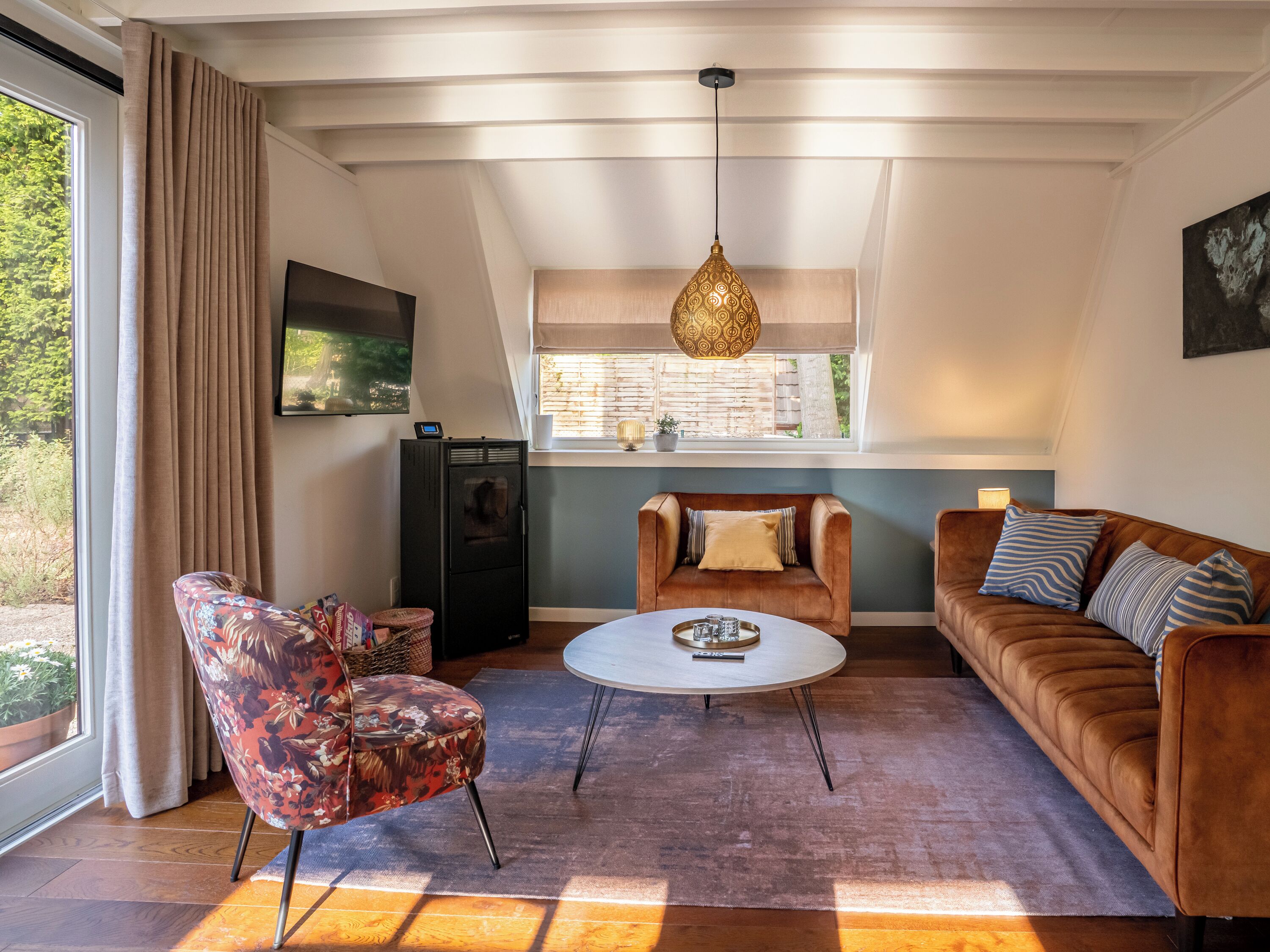 Uma sala de estar moderna com sofá, poltrona e mesa de centro. Uma janela grande oferece luz natural e vista para o verde lá fora.